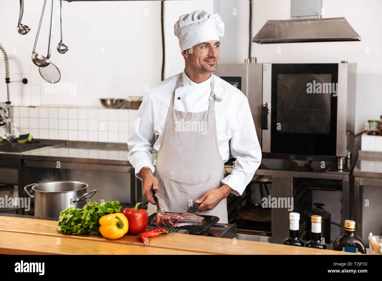Image of male chief in white uniform cooking meal with meat and ...
