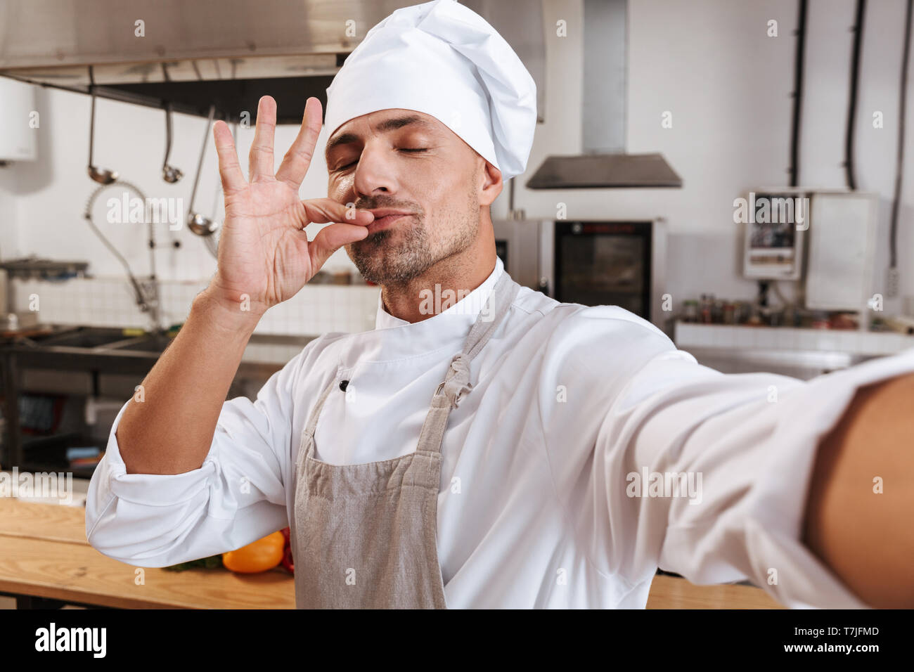 Photo of caucasian male chief in apron taking selfie while standing at ...