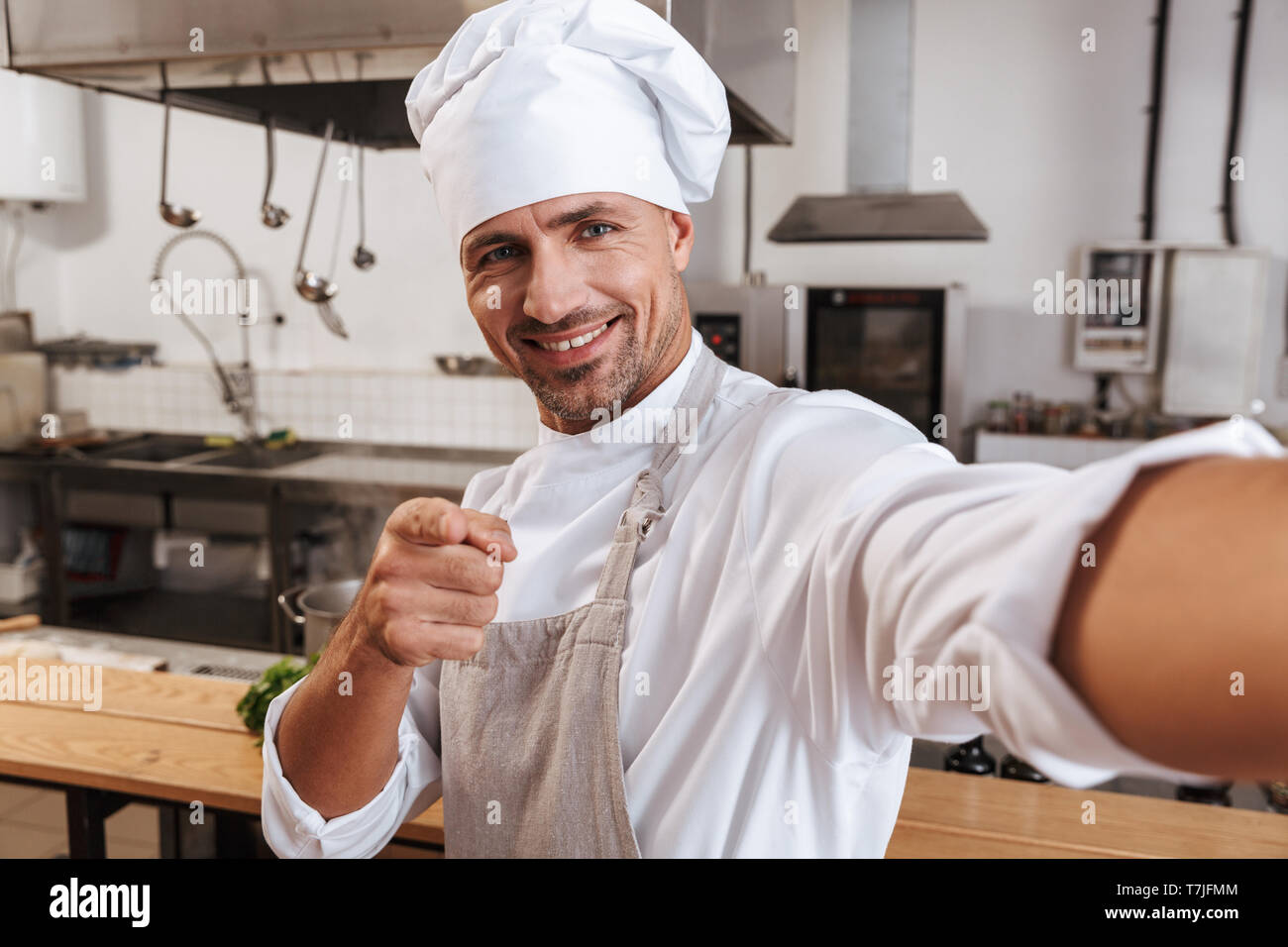 Photo of professional male chief in apron taking selfie while standing ...