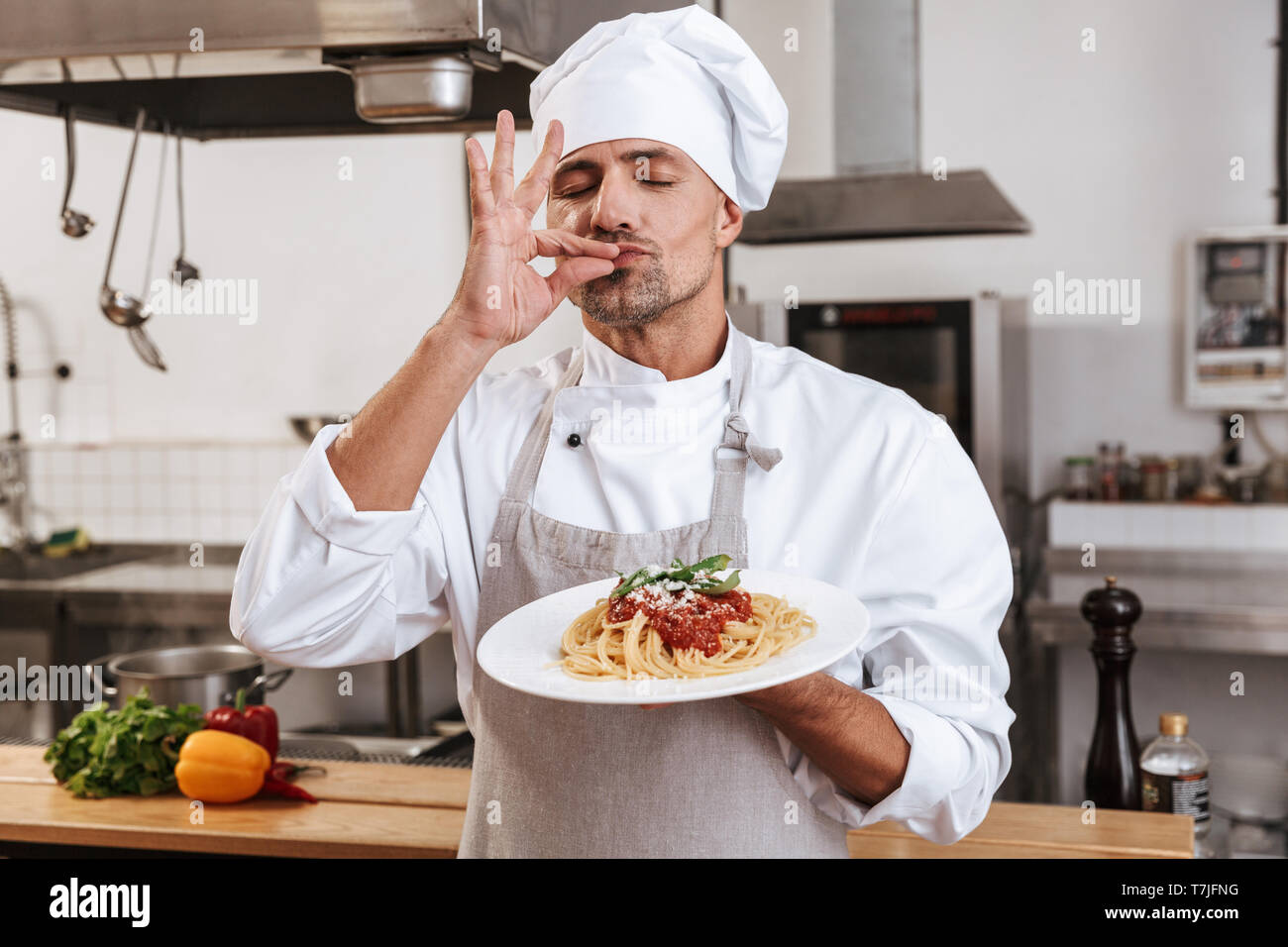 Photo of handsome male chief in white uniform holding plate with pasta ...