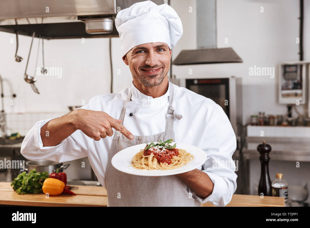 Photo of happy male chief in white uniform holding plate with meal ...