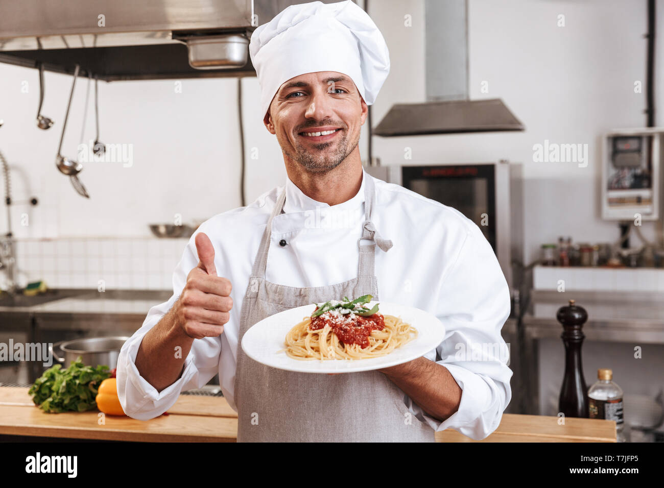 Photo of smiling male chief in white uniform holding plate with meal ...