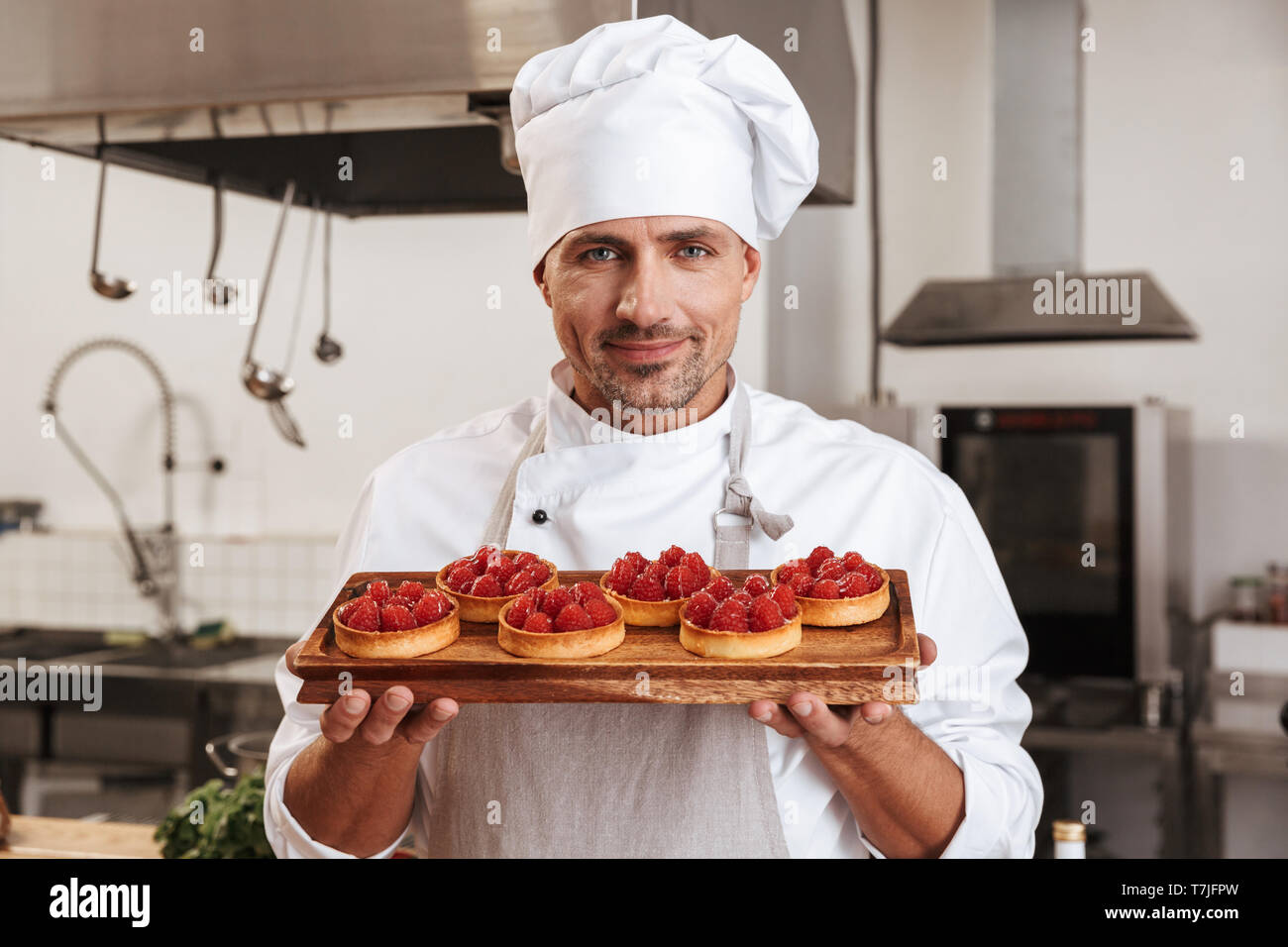 Photo of adult male chief in white uniform holding plate with cakes ...