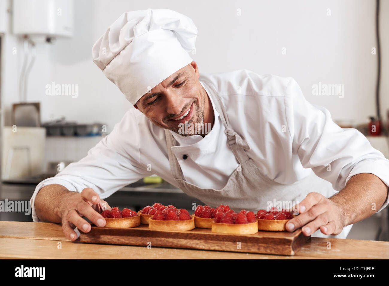 Photo of attractive male chief in white uniform holding plate with ...