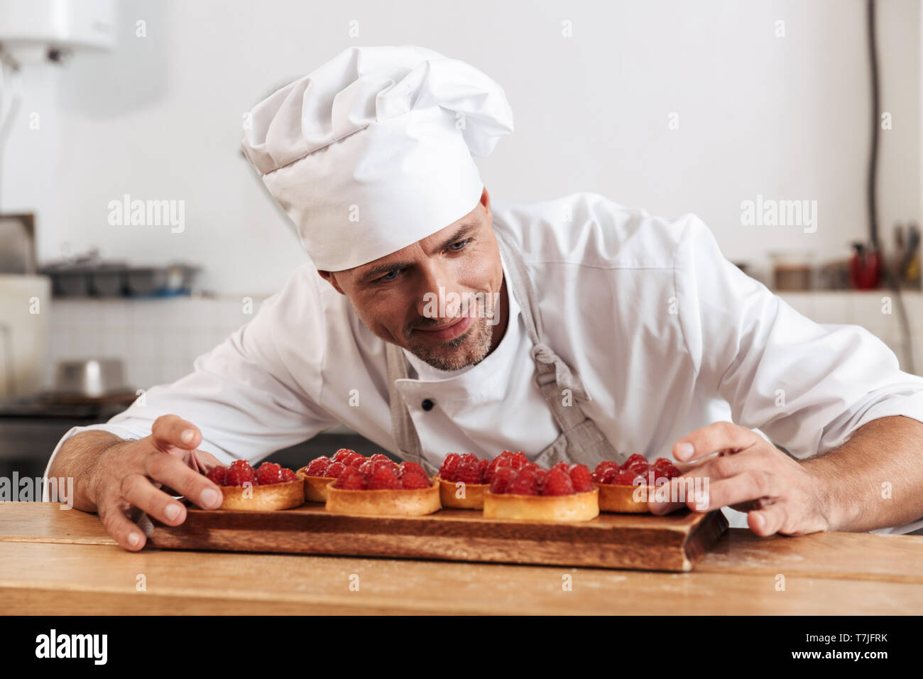 Photo of cheerful male chief in white uniform holding plate with cakes ...