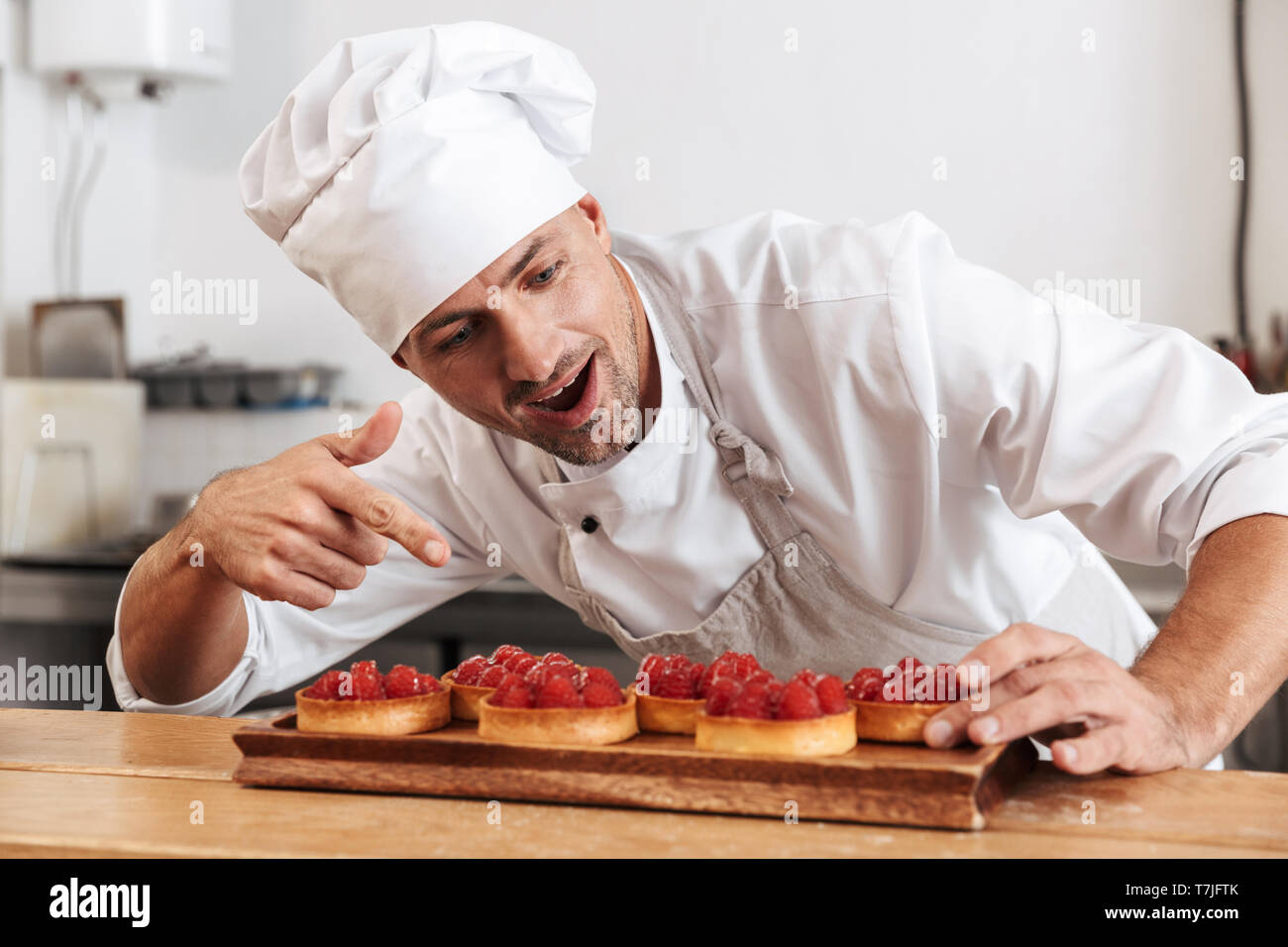 Photo of pleased male chief in white uniform holding plate with cakes ...