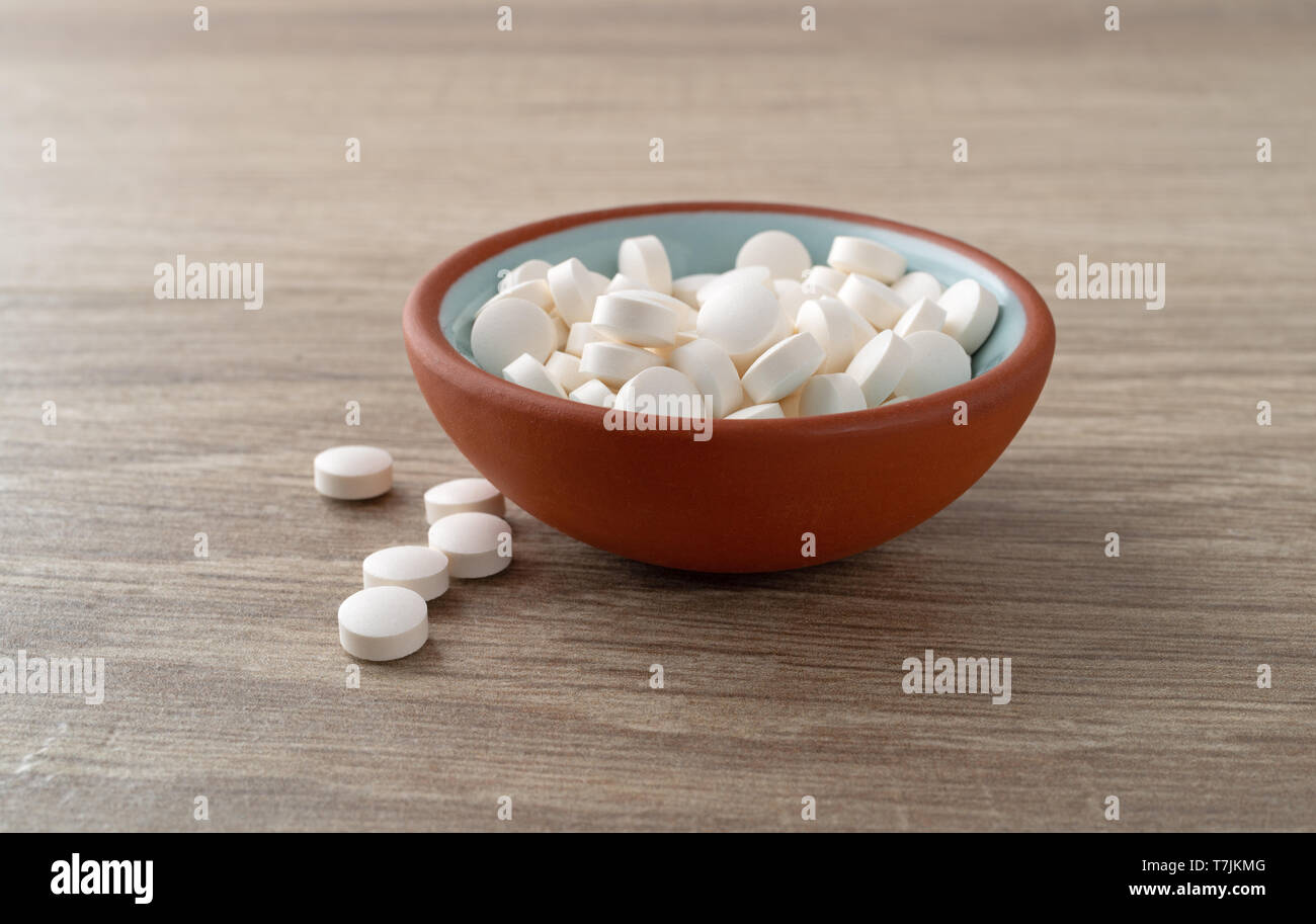 Side view of several DHEA pills in a small bowl and on a tile table top ...