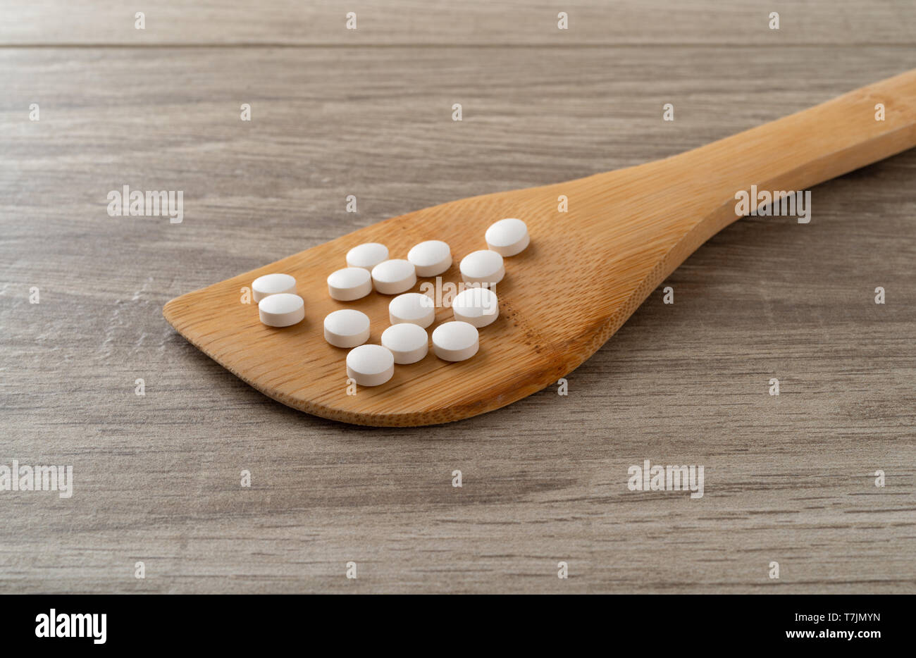 Side view of several DHEA pills on a wood spoon atop a tile table top ...