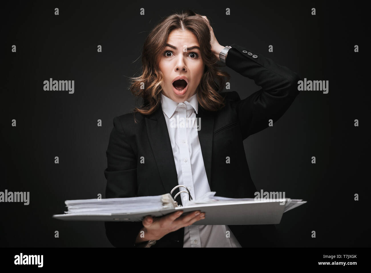 Portrait of a tired busy young businesswoman wearing formal suit standing isolated over black ...