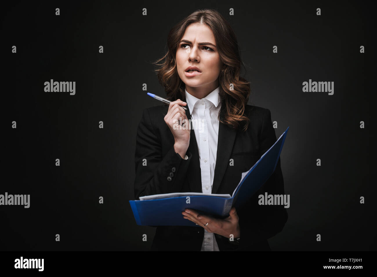 Portrait of a tired busy young businesswoman wearing formal suit standing isolated over black ...