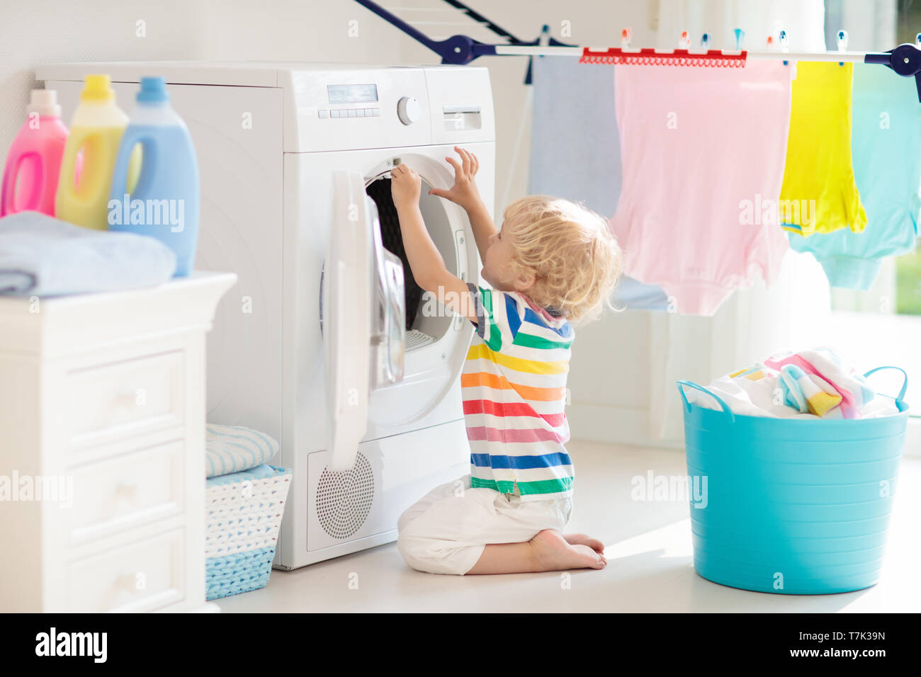 Child in laundry room with washing machine or tumble dryer. Kid helping ...