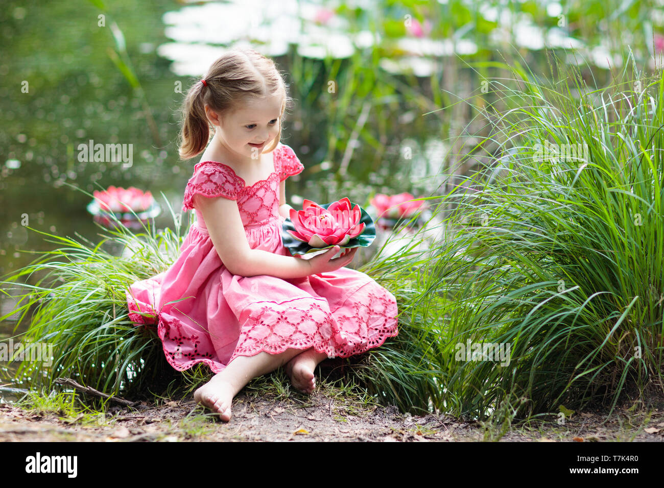 Child sitting at lake shore watching water lily flowers. Little girl ...
