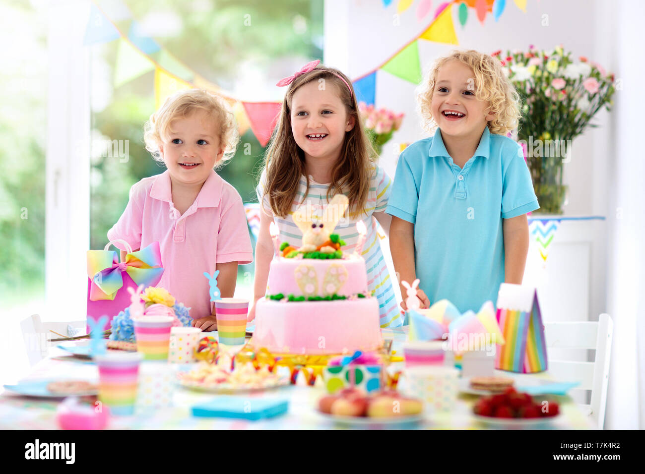 Kids birthday party. Children blow out candles on pink bunny cake ...