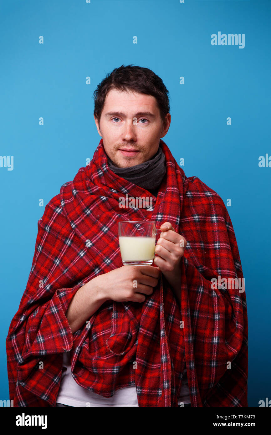 A wrapped in a blanket sick man is standing with cup of medicine in his ...