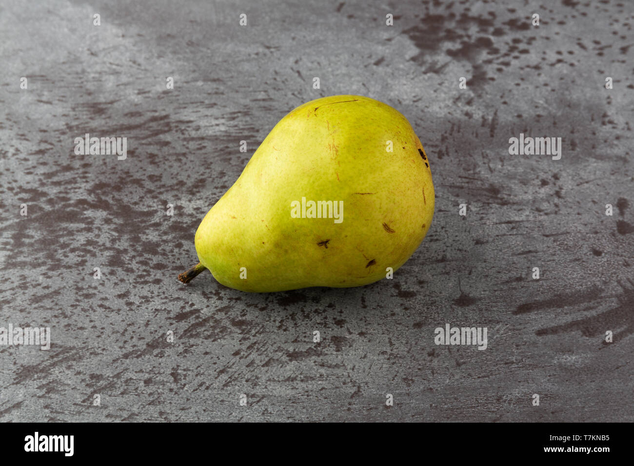 Side view of a single ripe green anjou pear on a gray mottled ...