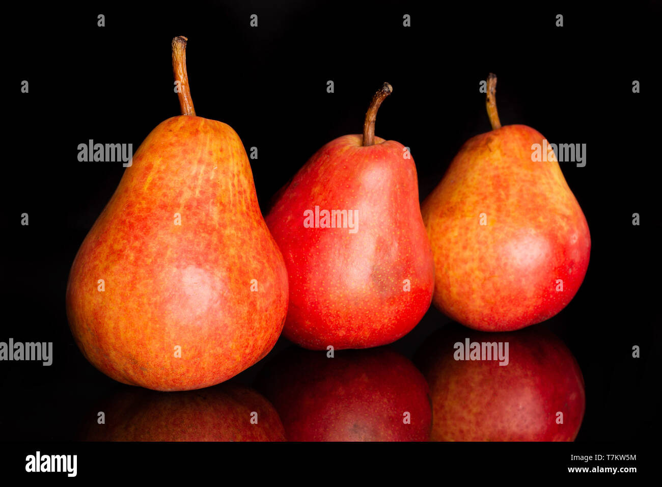 Group of three whole fresh red pear in row isolated on black glass ...