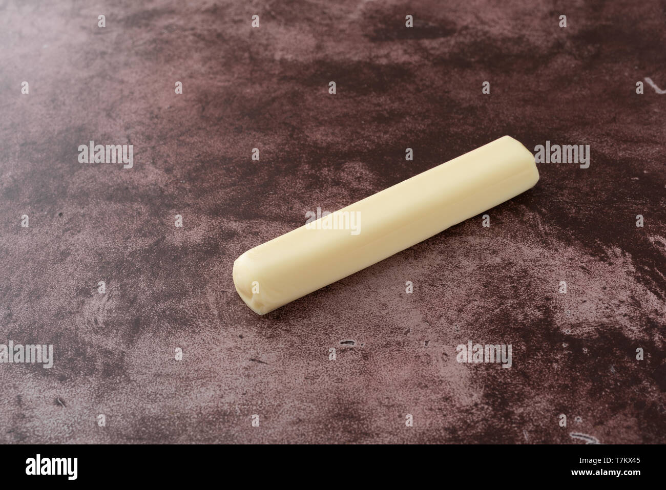 Side view of a single mozzarella snack string cheese stick on a red ...