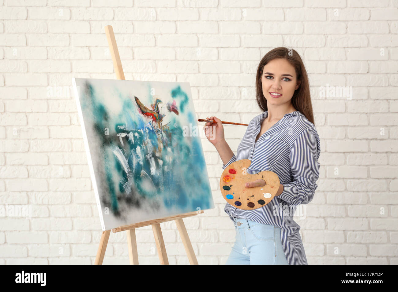 Young female artist with drawing easel against white brick wall Stock ...