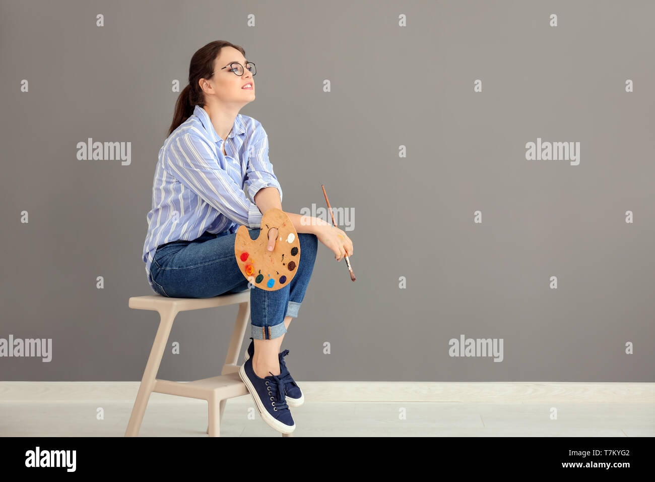Female artist sitting on stool near grey wall Stock Photo - Alamy