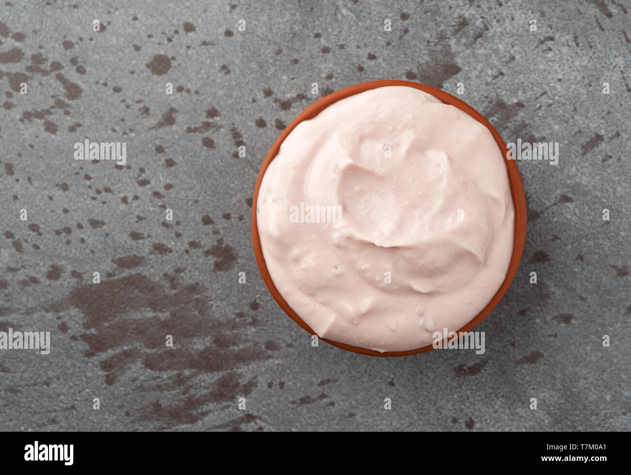 Overhead view of a small bowl of red raspberry yogurt on a gray table ...
