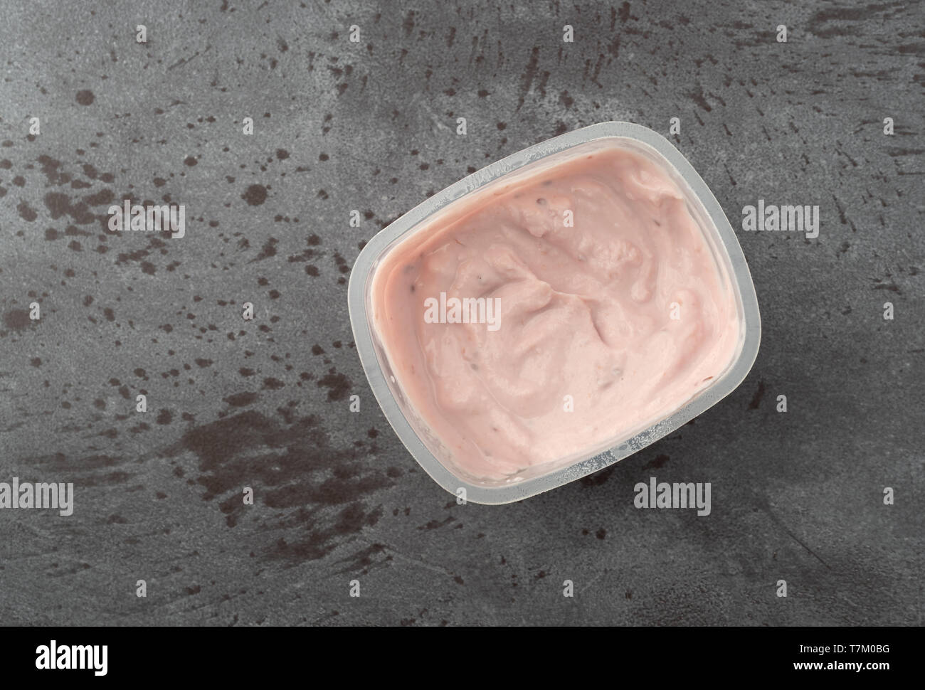 Overhead view of a small container of red raspberry yogurt on a gray ...