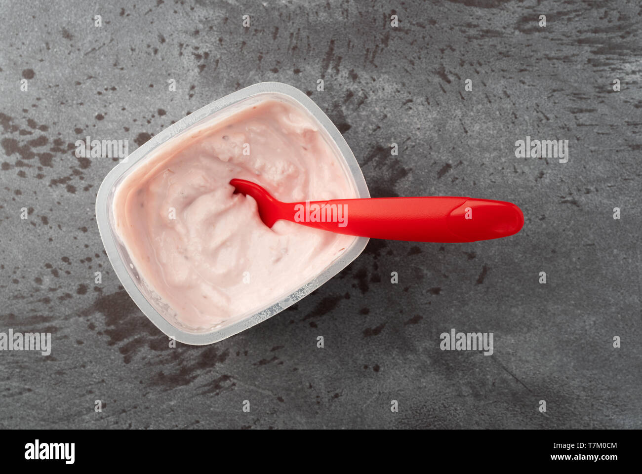 Overhead view of a small container of red raspberry yogurt with a spoon ...