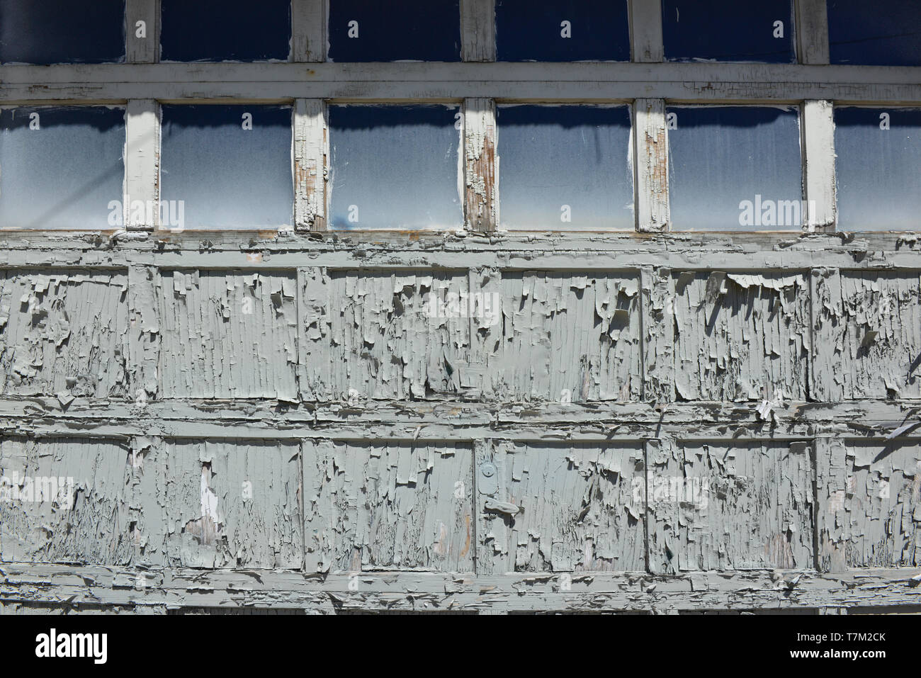 A weathered and paint peeling wooden garage door with dirty windows in ...