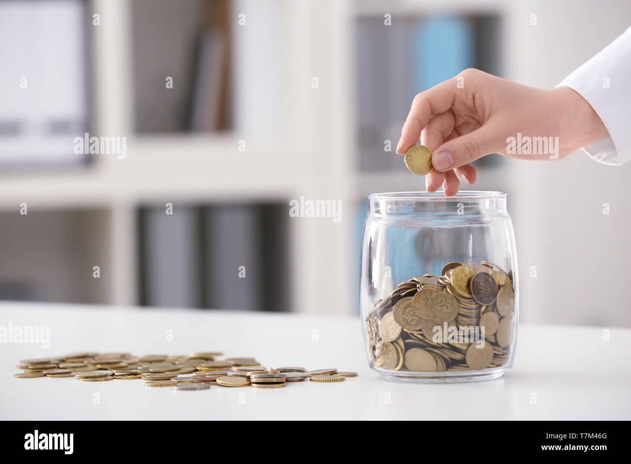 Woman putting coins into glass jar on table. Savings concept Stock ...