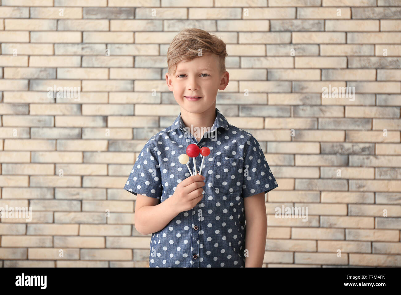 Cute little boy with lollipops near brick wall Stock Photo - Alamy