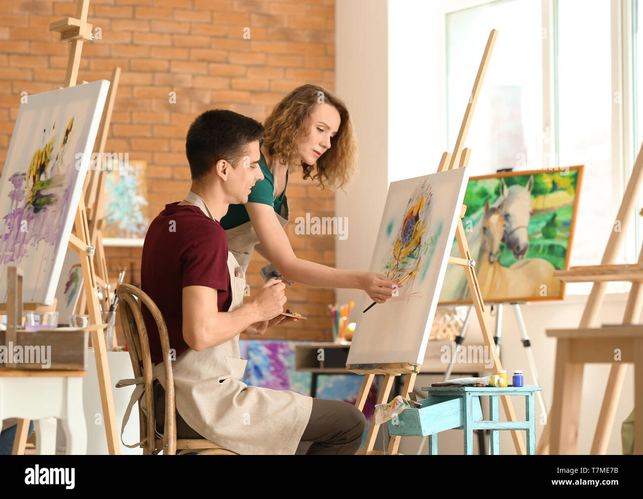 Female teacher helping her student during classes in school of painters ...