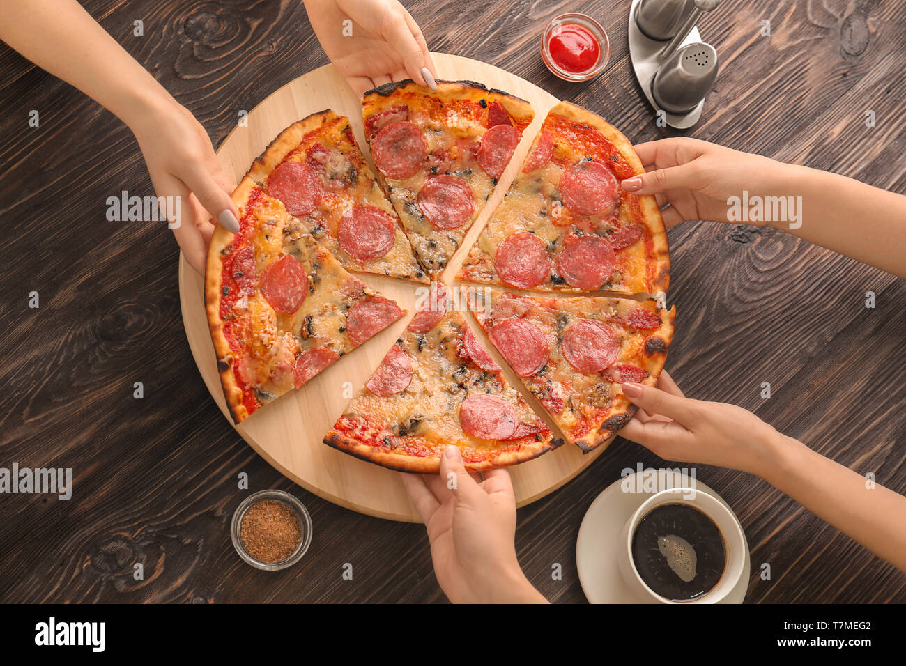 Young women taking pieces of pepperoni pizza from wooden plate Stock ...