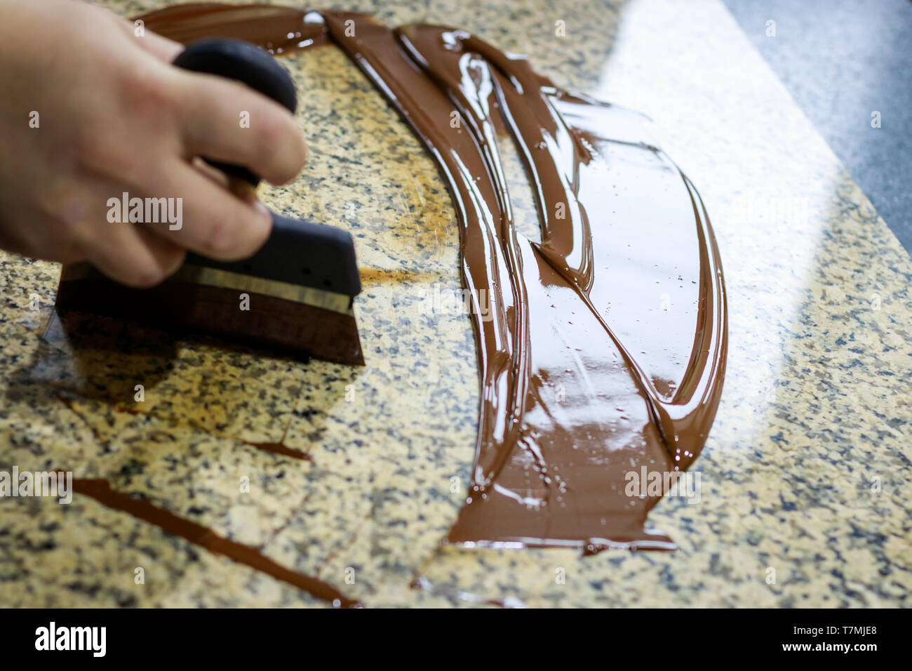 Liquid tempered chocolate applied in a thin layer on a granite table ...