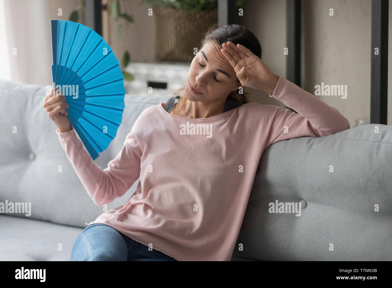 Woman feels discomfort from heat waving blue fan to cool Stock Photo ...