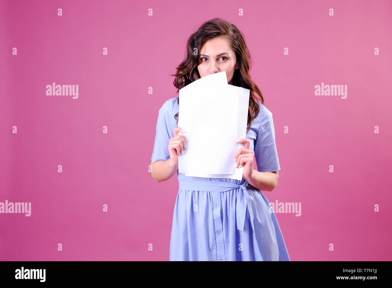 Young caucasian brunette woman holding paper over pink background ...