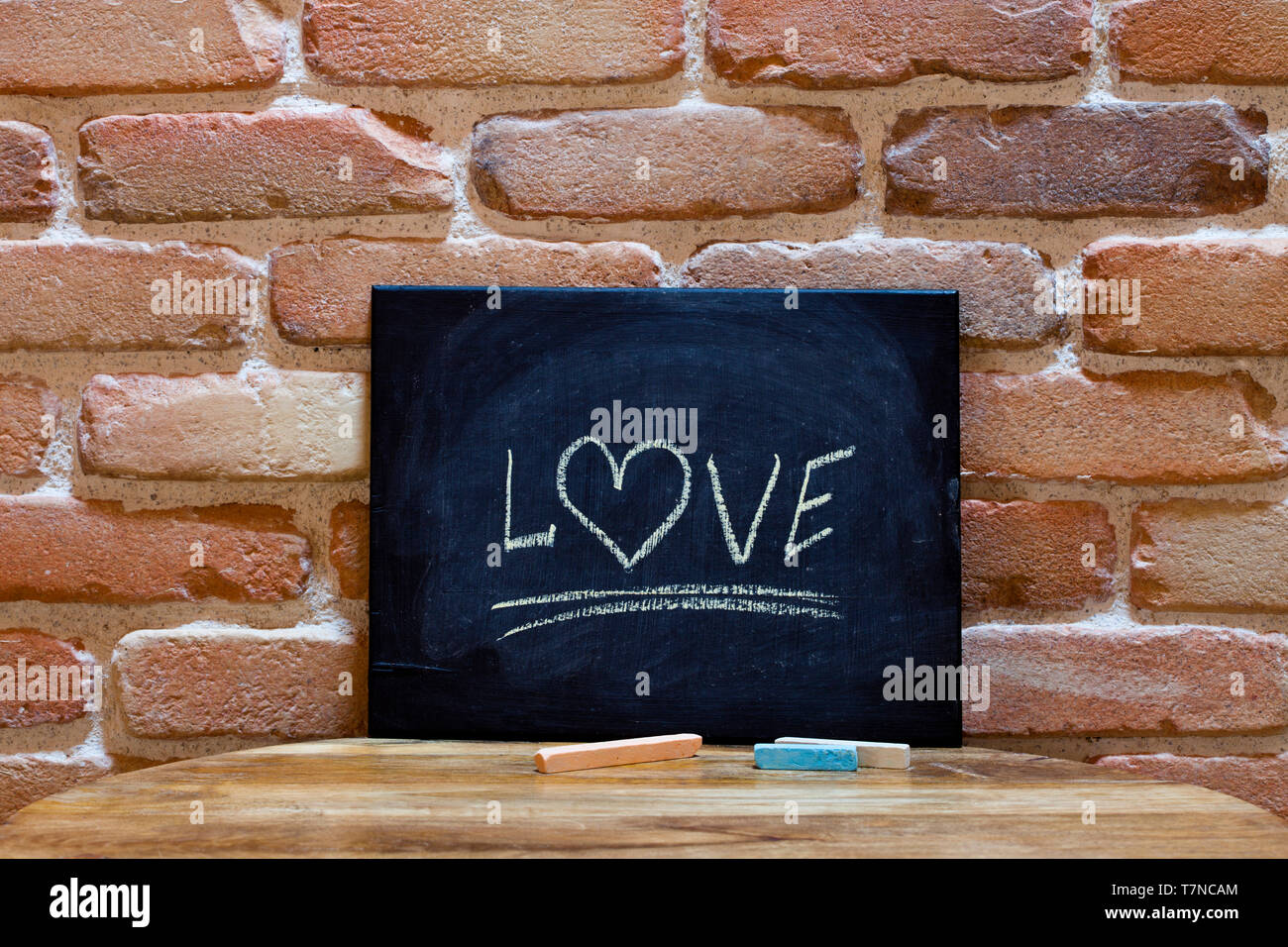 Black board with the word "Love" drown by hand on wooden table on brick ...