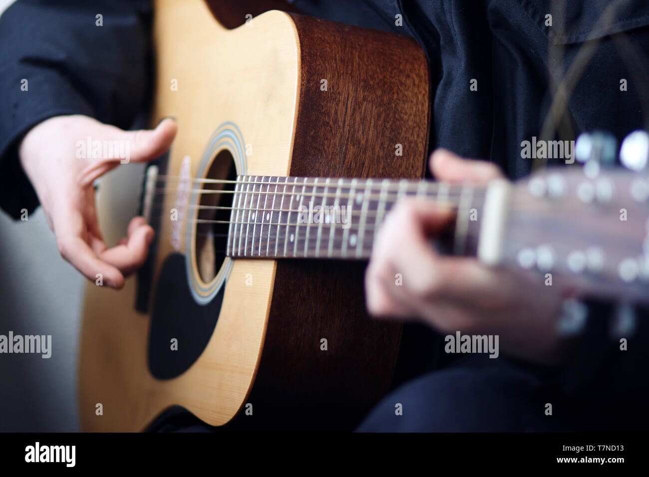 A man in dark clothes playing acoustic wooden six-string guitar ...