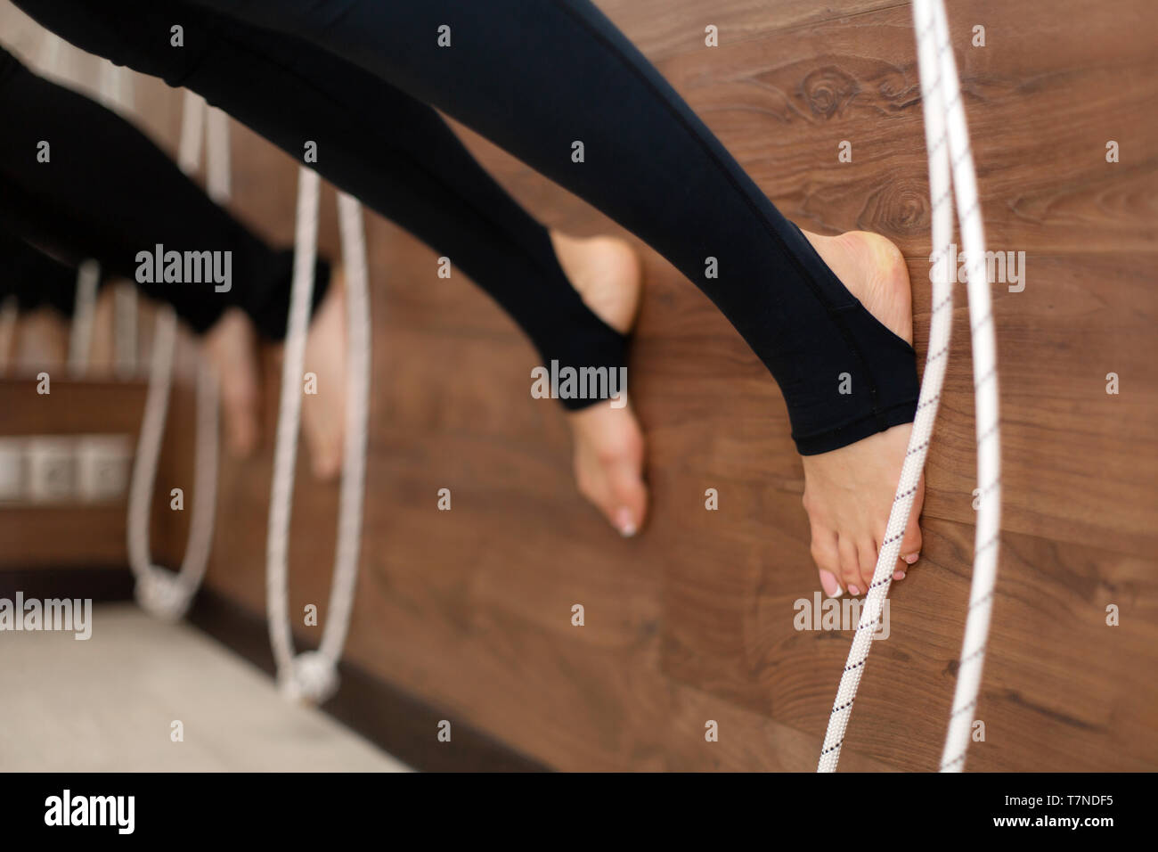 close up legs on wall while woman practicing yoga on ropes stretching ...
