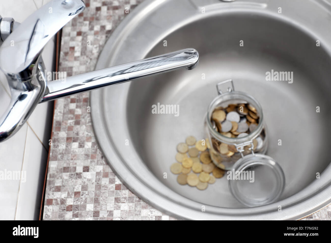 Metal tap and glass jar with coins in sink. Water saving concept Stock ...