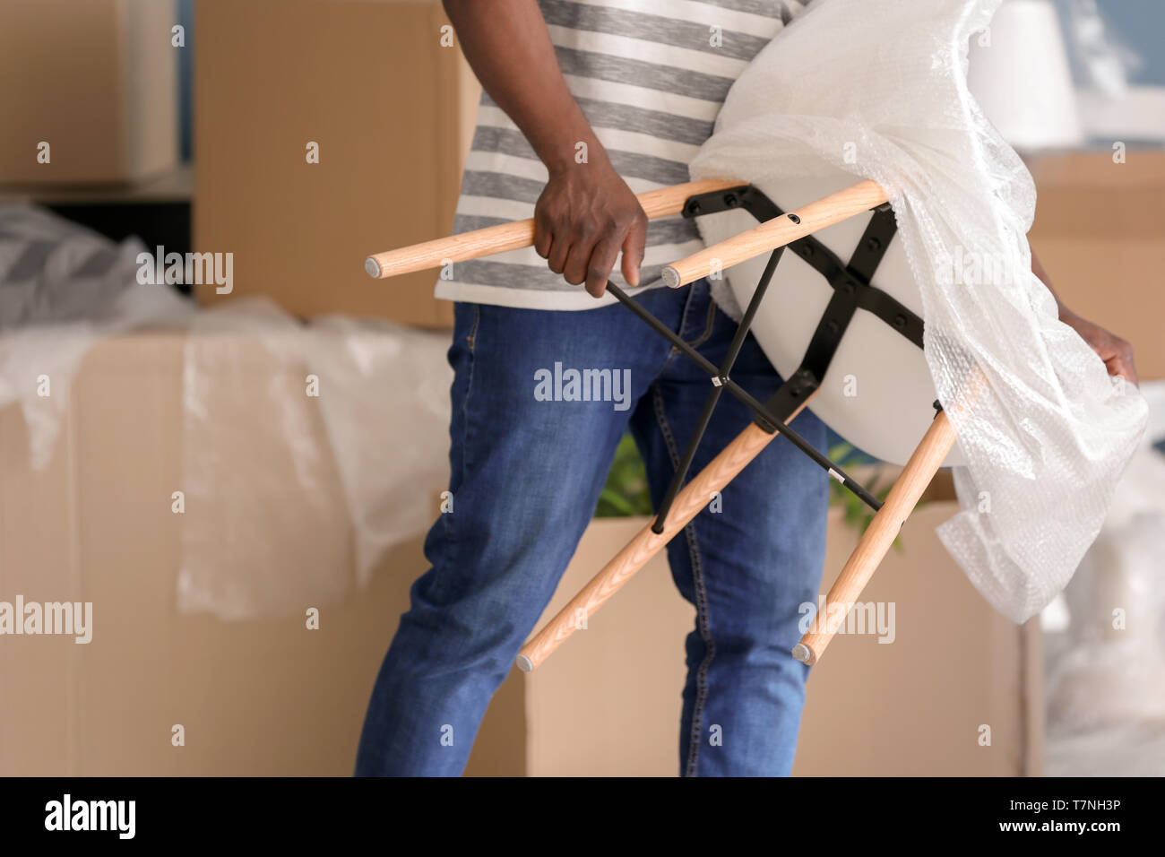 African-American man unpacking chair indoors. Moving into new house ...