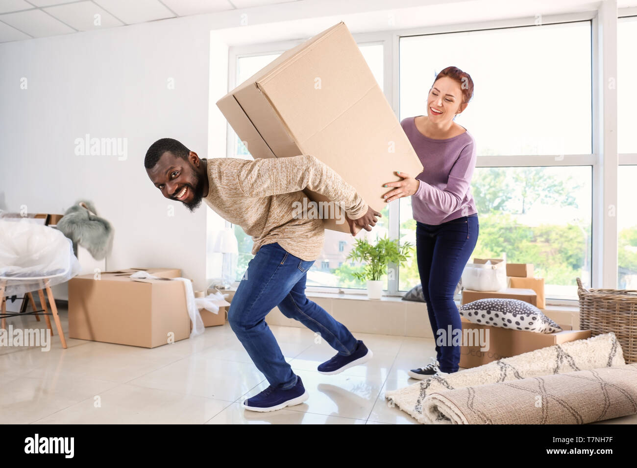 Interracial couple carrying big box in room. Moving into new house ...