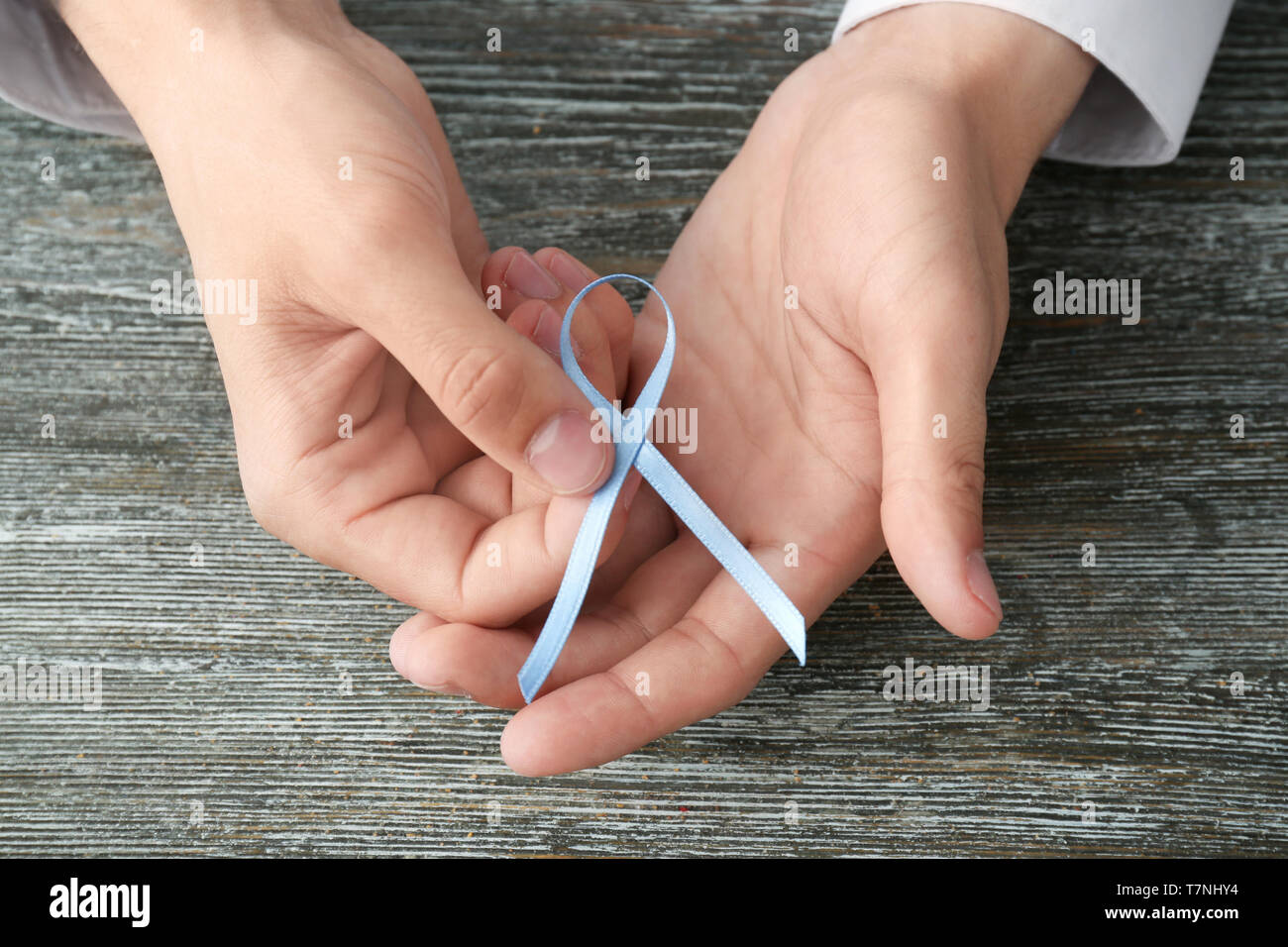 Male hands with blue ribbon on wooden background. Prostate cancer ...