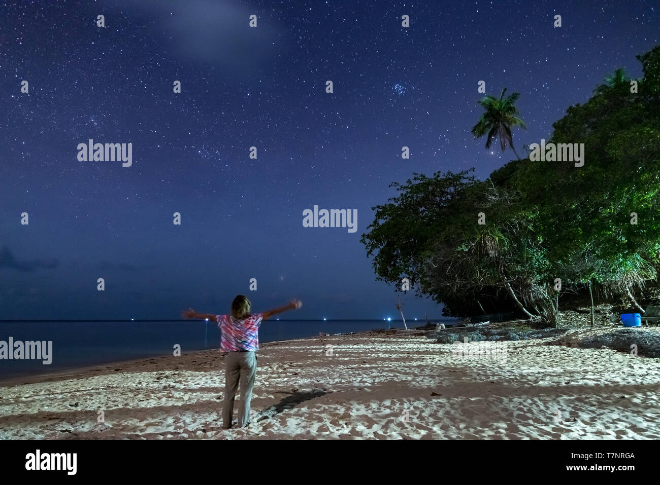 Woman looking at stars and milky way on sand beach, torch light on ...