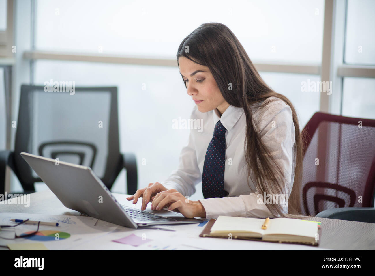 Serious young businesswoman typing on laptop in a bright modern office ...