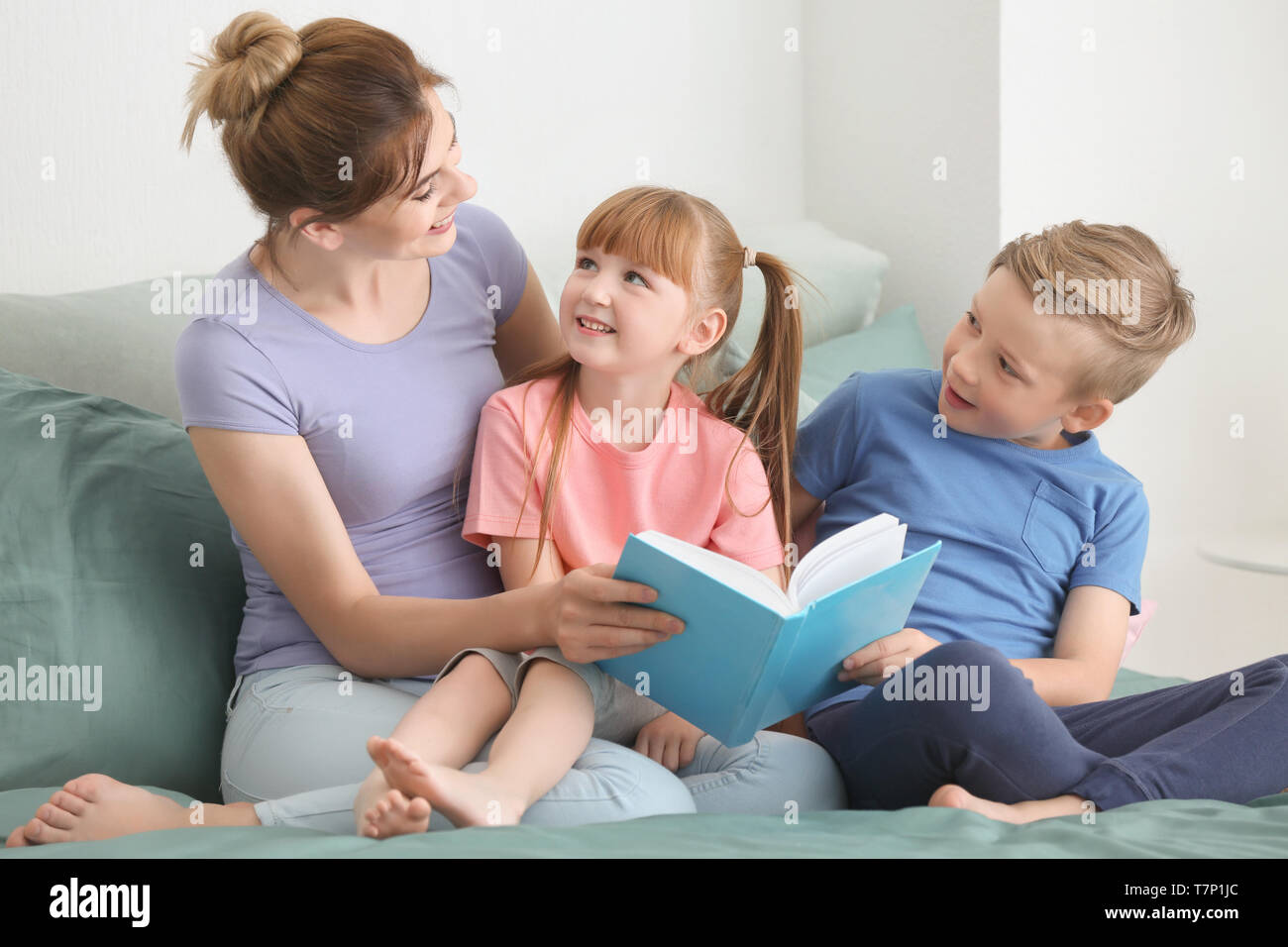 Mother and her children reading book together at home Stock Photo - Alamy