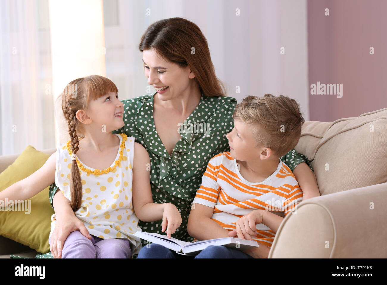 Mother and her children reading book together at home Stock Photo - Alamy