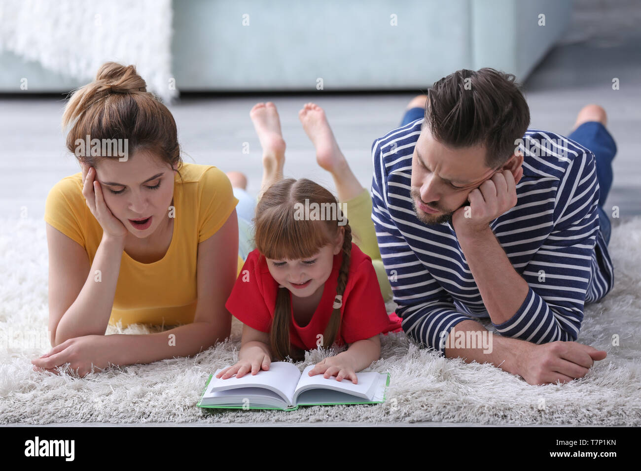 Parents and their daughter reading book together at home Stock Photo ...