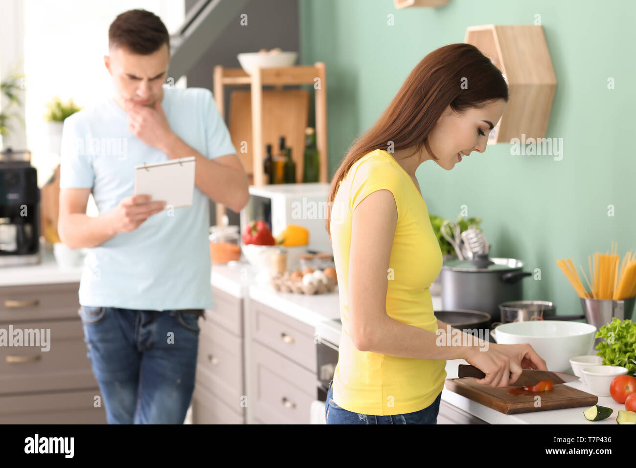 Young woman cooking while her husband reading recipe book in kitchen ...