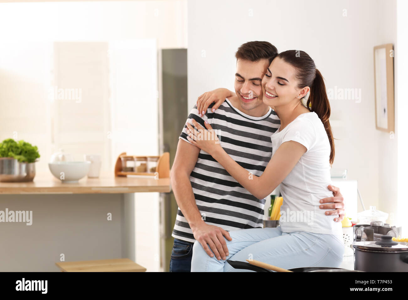 Young couple hugging while cooking together in kitchen Stock Photo - Alamy