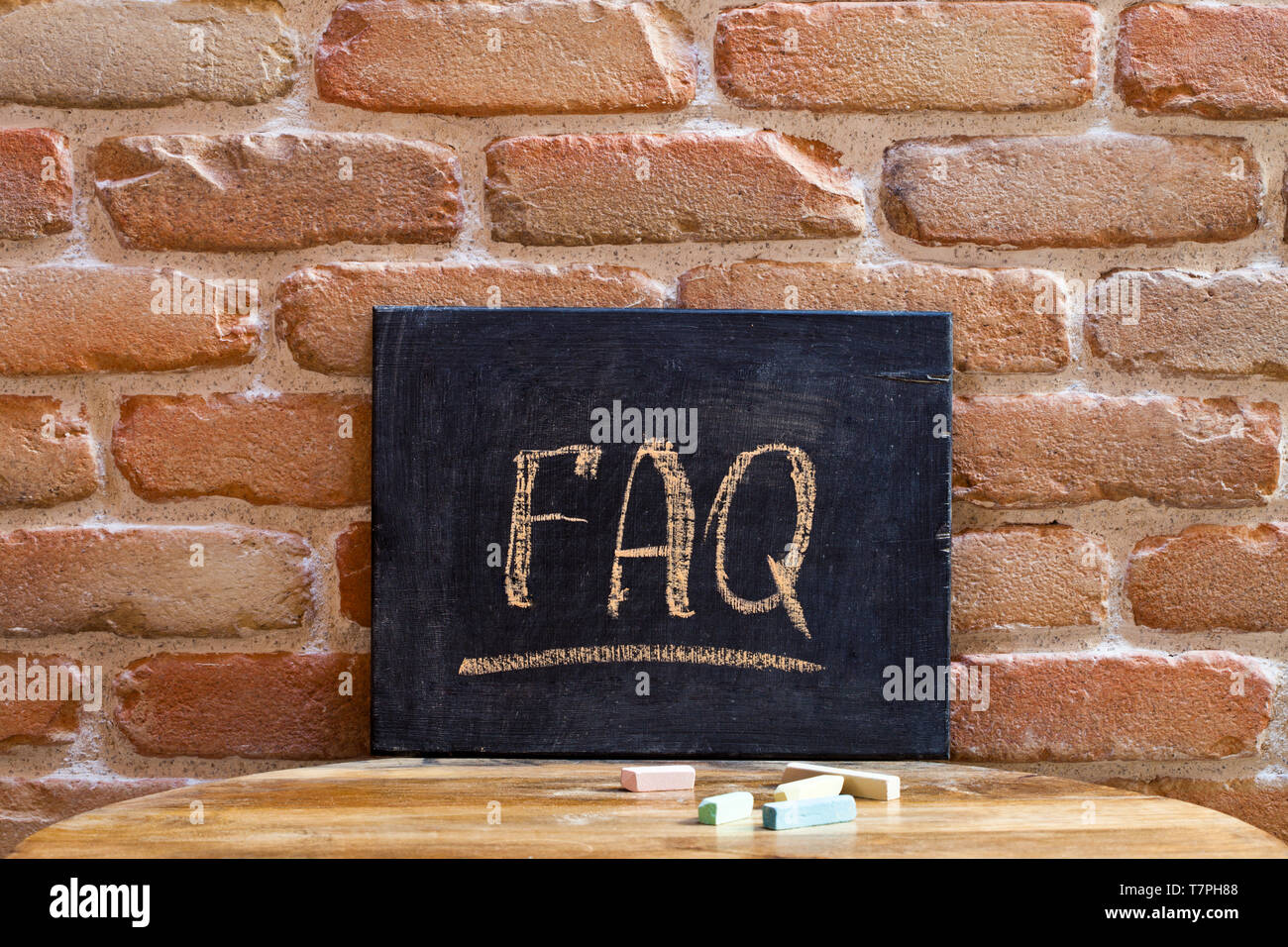 Black board with the word FAQ drown by hand on wooden table on brick ...