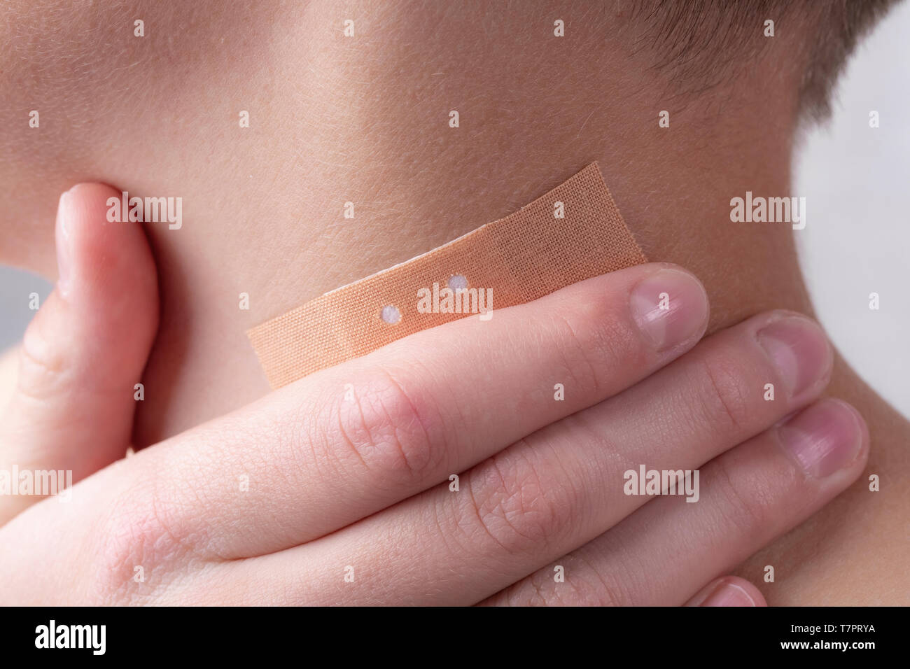 Adhesive plaster on the neck of a teenager on a wound. Hand touches a ...